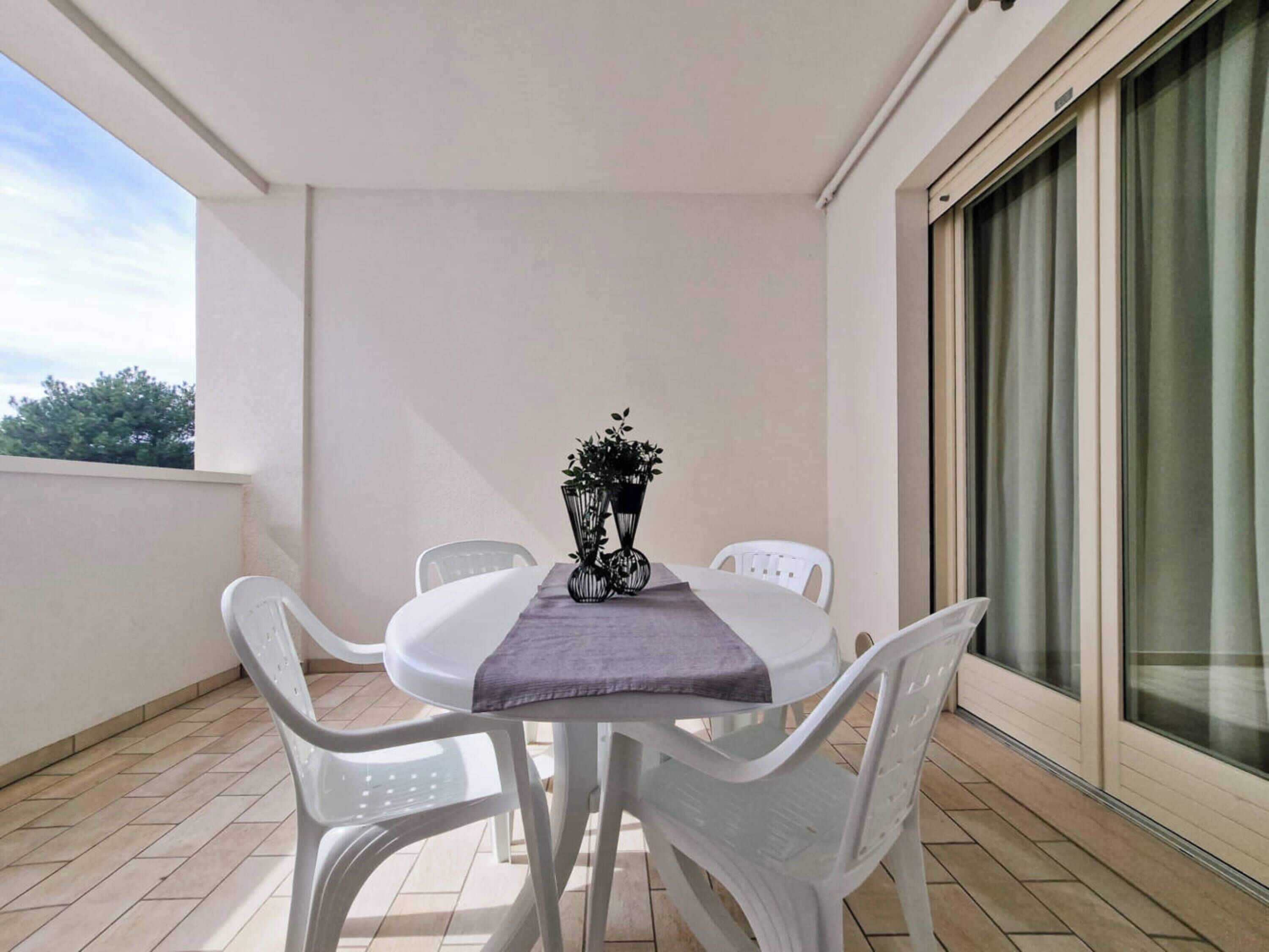 Uma varanda com uma mesa redonda, cadeiras brancas e toalha de mesa roxa.