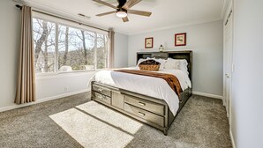 Quarto com cama, ventilador de teto, janela com cortinas e vista para árvores.