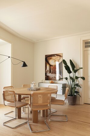 Uma área de refeições com uma mesa de madeira, cadeiras de vime, uma planta em vaso e um quadro na parede.
