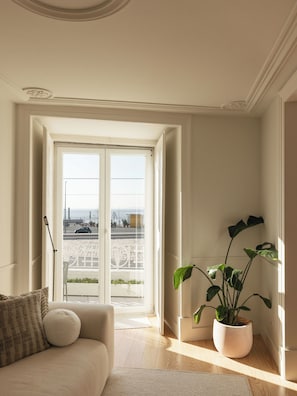 Quarto com uma grande porta de vidro deslizante que dá para uma varanda, uma planta em vaso e um sofá com almofadas.
