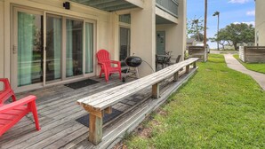 Uma área externa coberta com deck de madeira, churrasqueira e uma cadeira Adirondack vermelha.