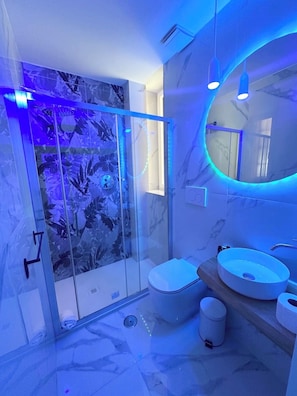Uma casa de banho moderna com cabine de duche em vidro, lavatório de mármore e espelho redondo.
