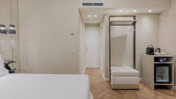 Quarto de hotel com cama, closet espaçoso, minibar e área de chuveiro.
