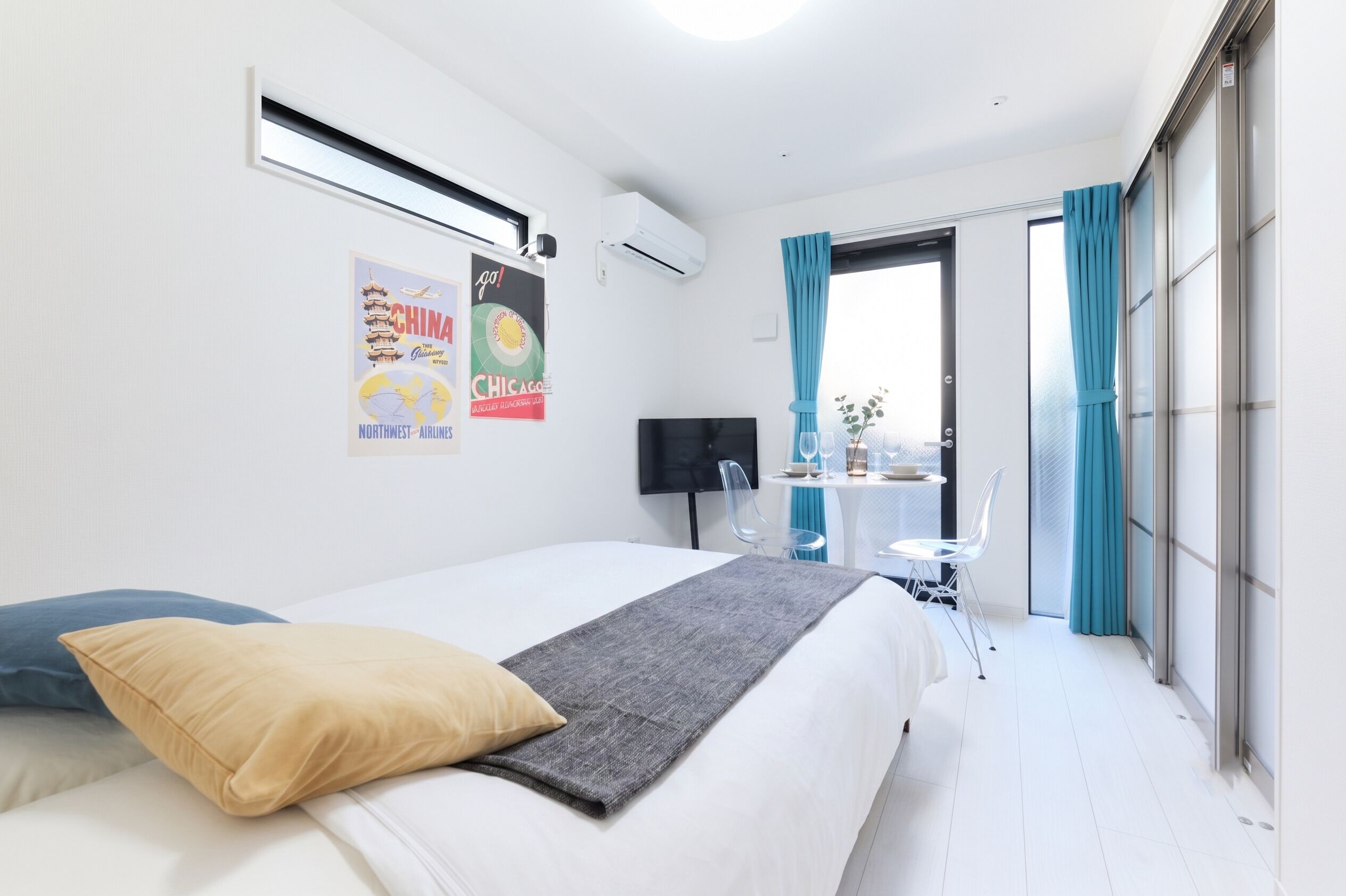 Quarto de hotel com cama, televisão, mesa pequena com cadeiras e varanda com cortinas.
