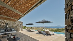 Área externa com paredes de pedra, piscina, espreguiçadeiras e guarda-sóis.