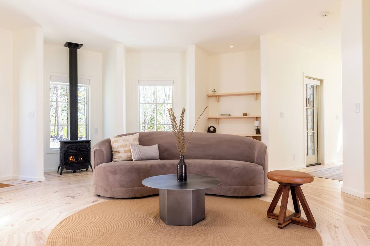 Uma sala de estar moderna com uma mesa redonda, um sofá, um banquinho de madeira e uma lareira.