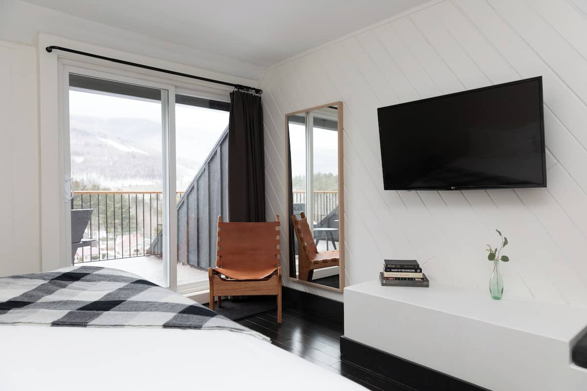 Quarto com cama, uma cadeira, uma TV e vista para o exterior.