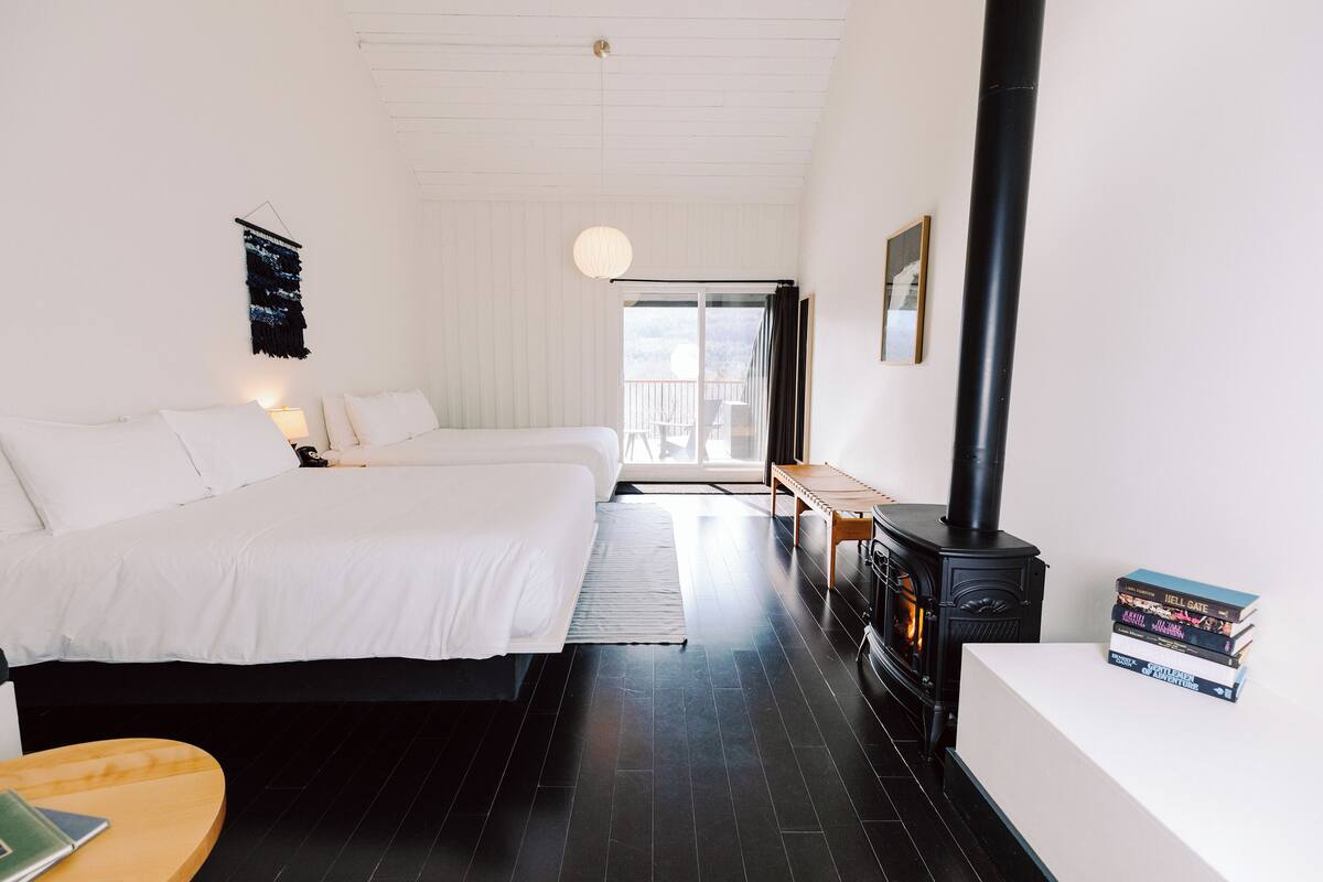 Quarto de hotel moderno com uma cama grande, uma mesa de madeira, uma estante e uma lareira a lenha preta.