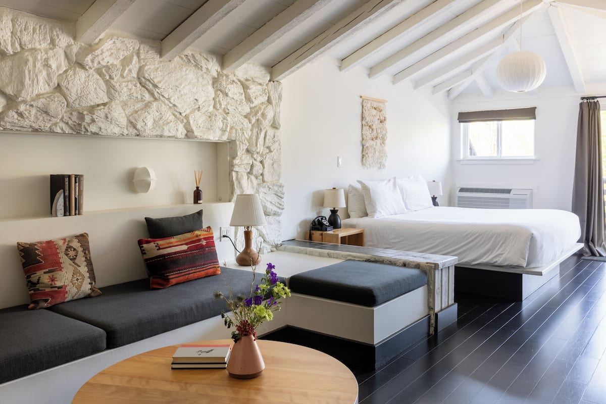 Quarto moderno com parede de pedra, cama, sofá e mesa de centro com um vaso.