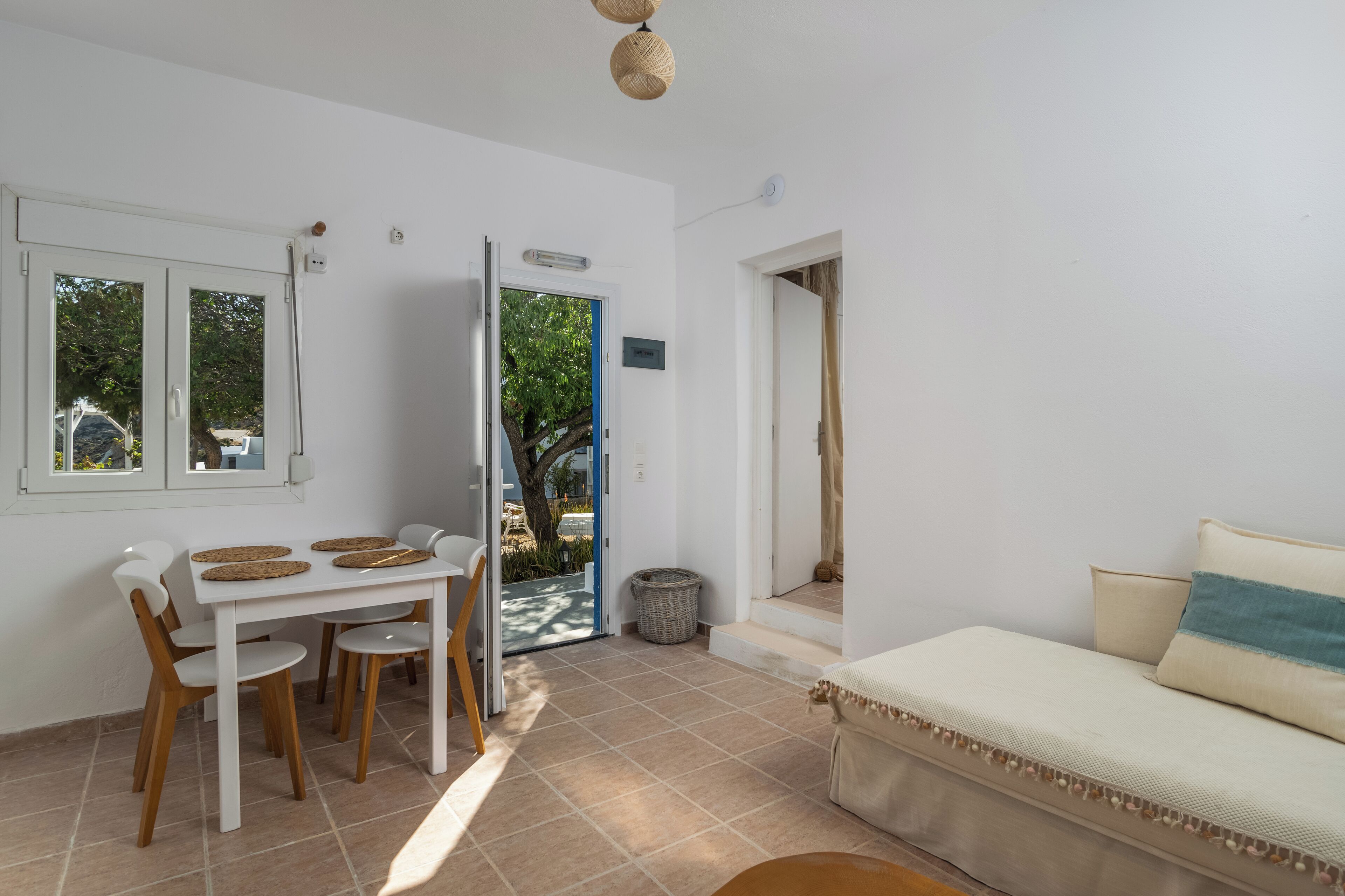Quarto com uma mesa e cadeiras brancas, um sofá e uma porta que dá para o exterior.