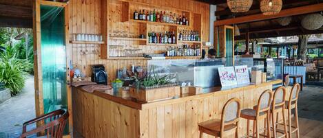 Uma área de bar com balcão, banquetas e prateleiras repletas de garrafas e copos.