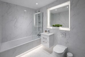 Casa de banho moderna com cabine de duche em vidro, toucador branco com gavetas, sanita e espelho grande com planta.