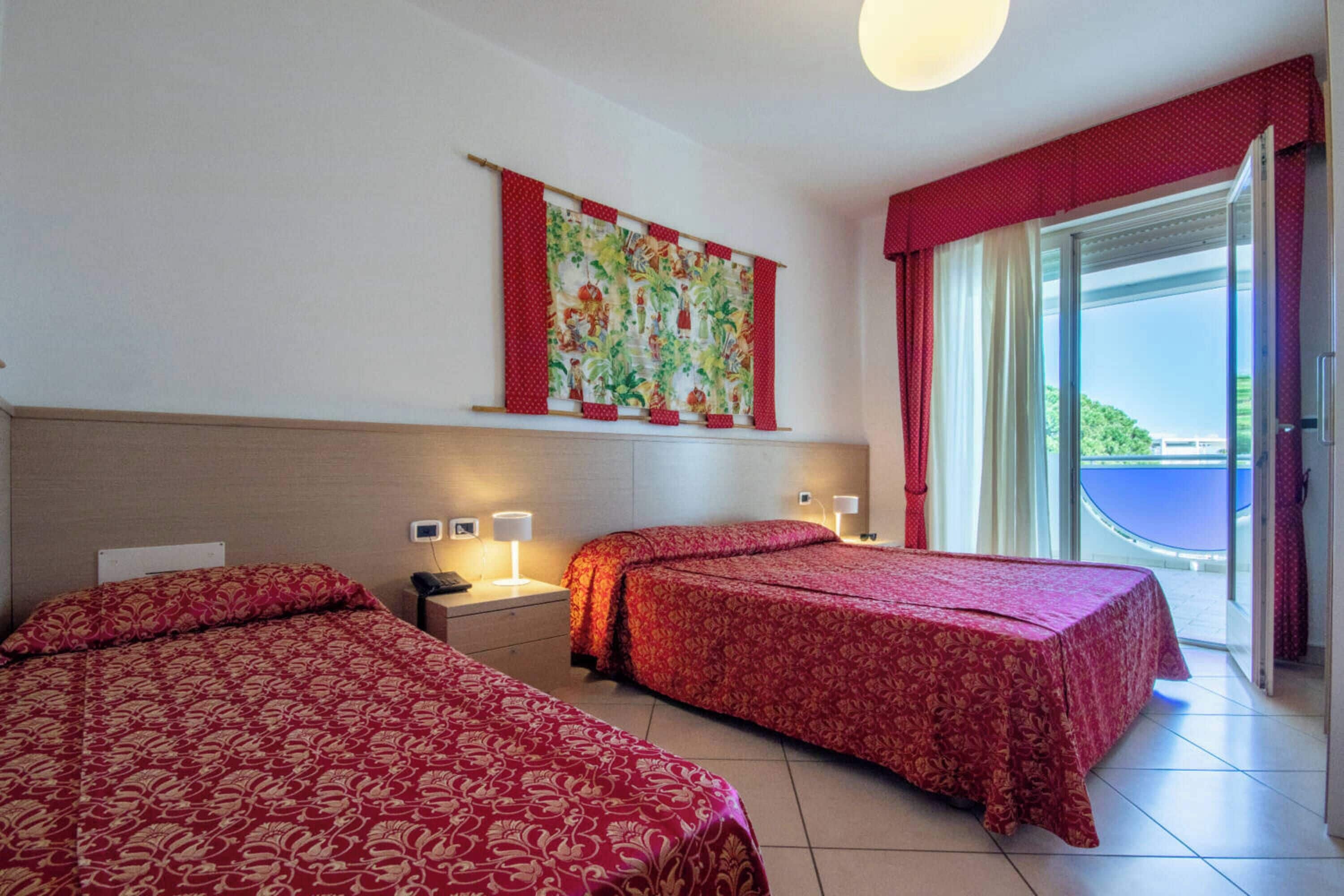 Quarto de hotel com duas camas, uma janela grande e uma vista, e uma obra de arte na parede.