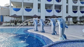 Piscina com estátuas de golfinhos e guarda-sóis.