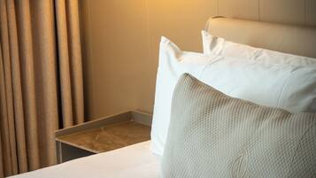 Cama bem arrumada com lençóis brancos e almofada texturizada, mesa de cabeceira com abajur e parede de painel de madeira.