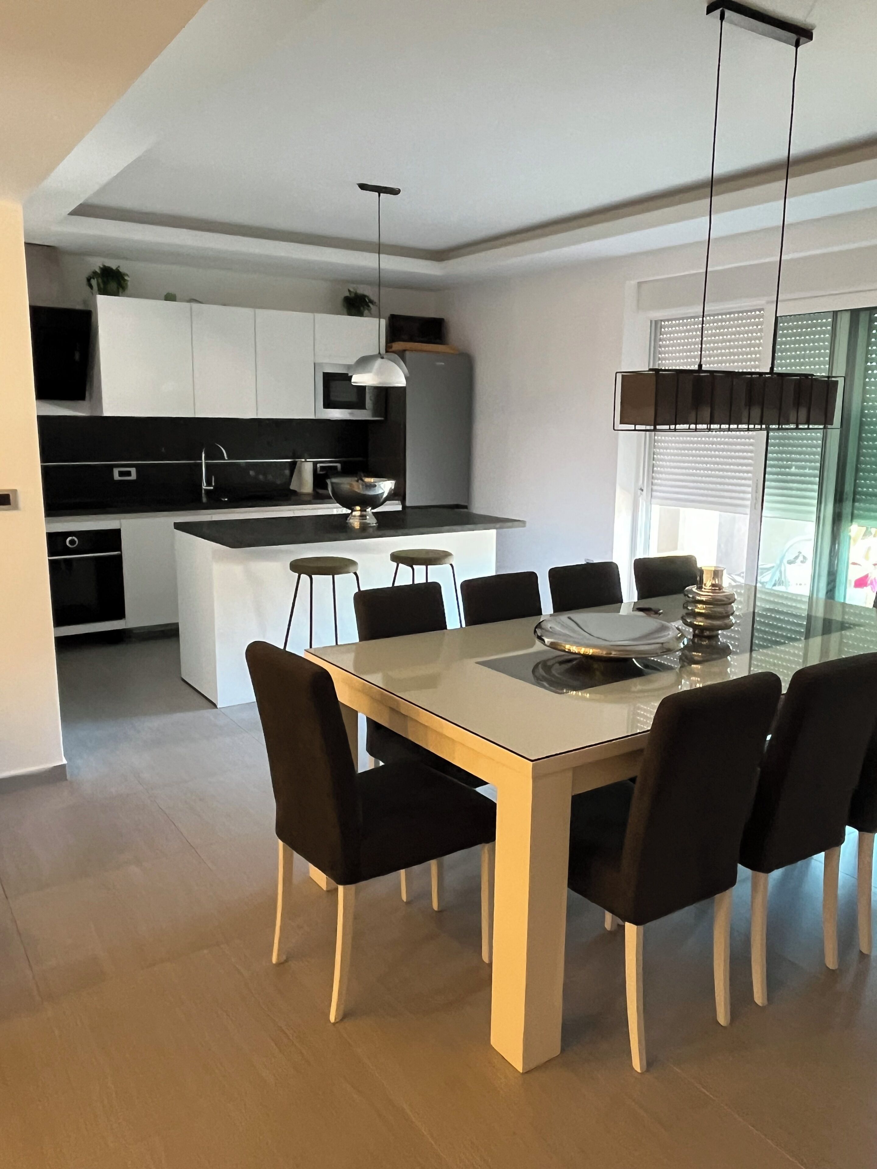 Uma cozinha moderna com armários brancos, bancada preta e uma ilha central com banquetas.