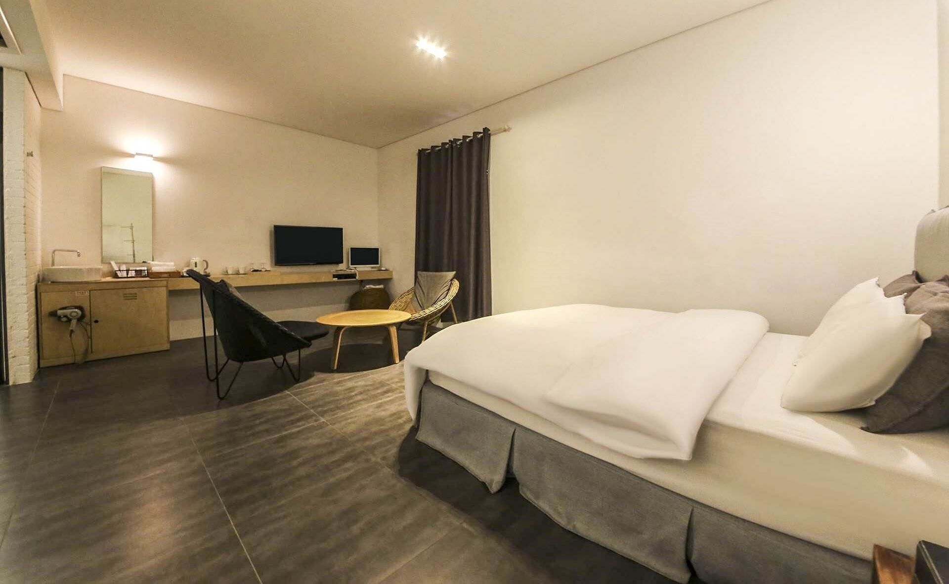 Quarto de hotel com cama, escrivaninha com computador, cadeira, televisão e banheiro.