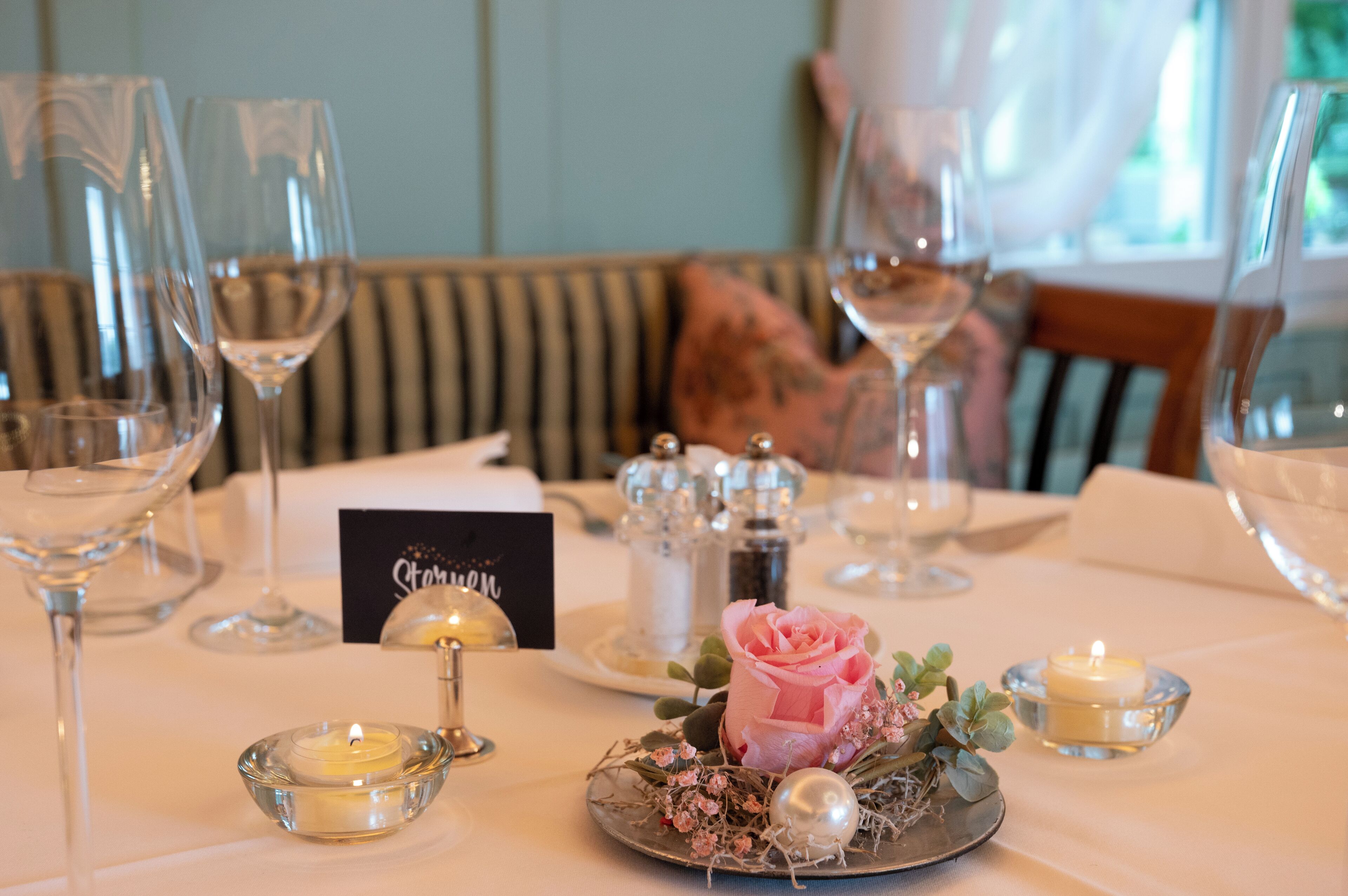 Uma mesa de jantar posta com taças de vinho, um arranjo de rosas, velas e um cardápio.