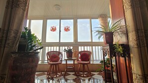 Quarto banhado por luz solar, com duas cadeiras de vime, uma mesa e plantas em vasos.