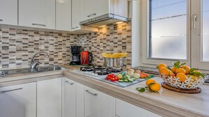 Uma cozinha moderna com armários brancos, painel de azulejos, fogão a gás e janela com vidro jateado.