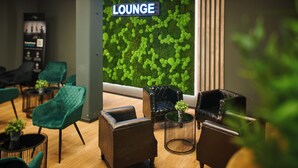 Espaço de descanso com cadeiras verdes, um letreiro 'Lounge' e uma parede verde com padrão de folhas.