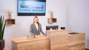 Uma mesa de receção com uma placa a indicar "hotel53nd FITNESS WELLNESS", um computador e um balcão de madeira.