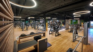 Uma academia com diversos equipamentos de exercício, piso de madeira e luminárias modernas.