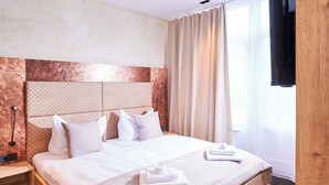 Uma cama grande com cabeceira de madeira, uma mesinha de cabeceira e uma televisão de tela plana na parede.
