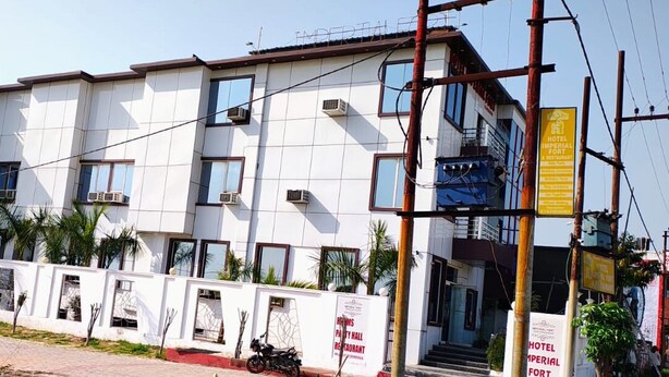 Um hotel de vários andares com fachada branca, unidades de ar condicionado e uma placa indicando ser o Imperial Fort Hotel.