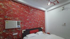 Quarto com parede estampada em vermelho, cama branca com duas almofadas, cabeceira vermelha e ar condicionado branco fixado na parede.