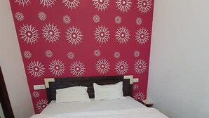 Cama bem arrumada em quarto com parede vermelha estampada e cabeceira preta.