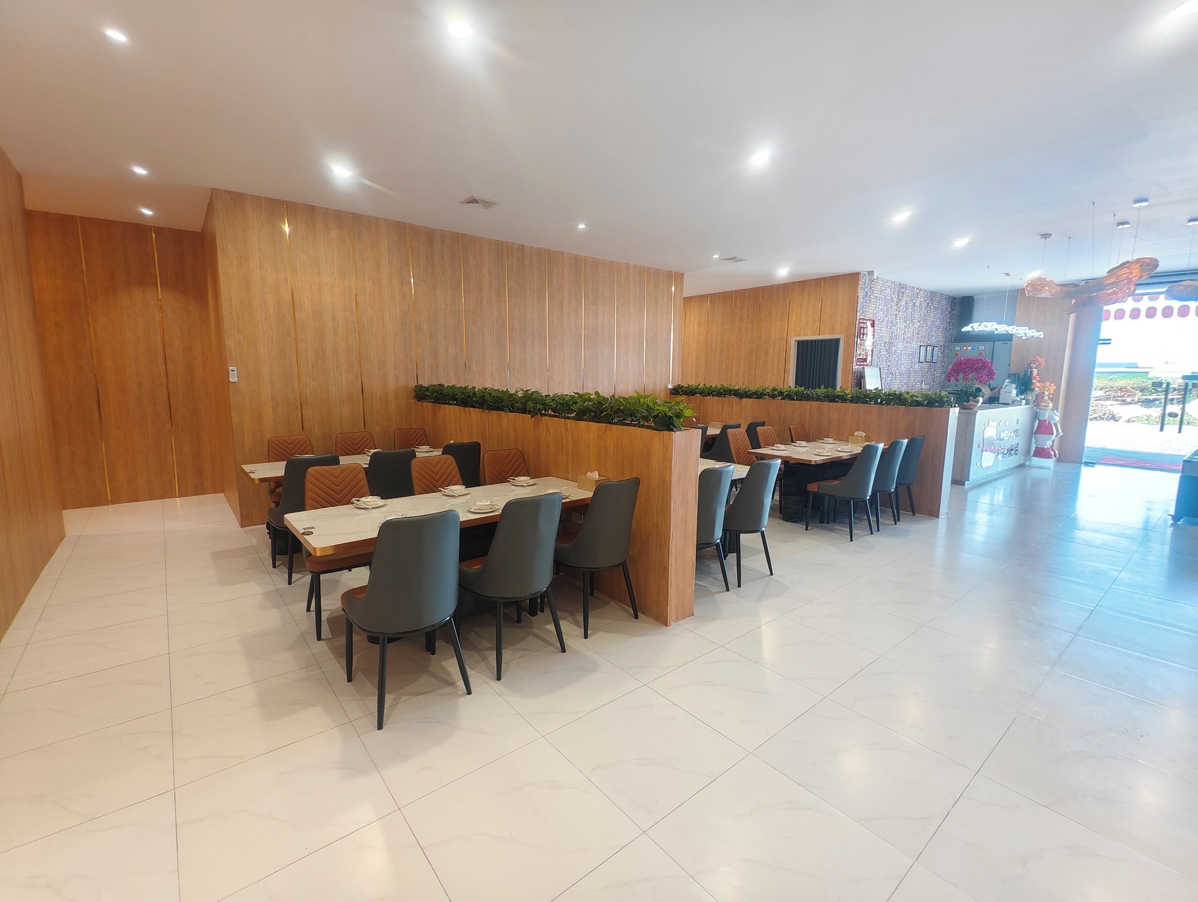 Um restaurante moderno com paredes revestidas de madeira, chão de azulejos e um balcão central com uma planta decorativa.