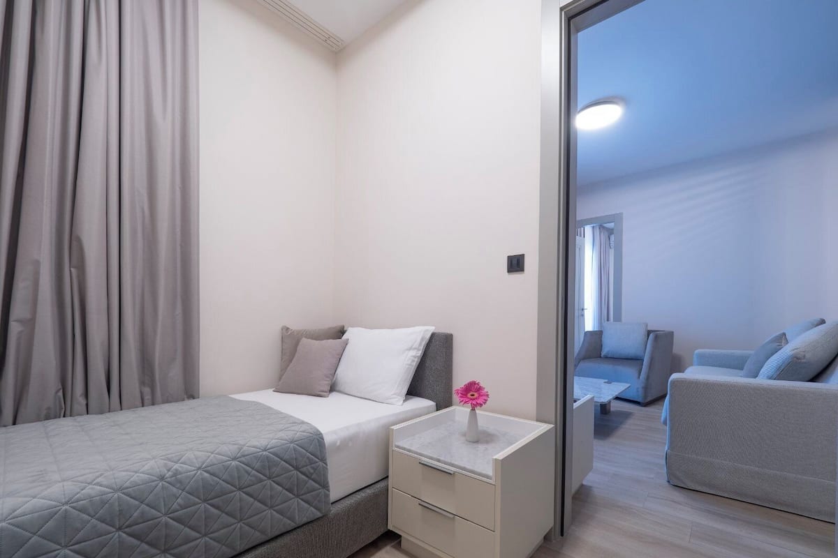 Quarto moderno com cama, mesa de cabeceira e vista para uma sala de estar.