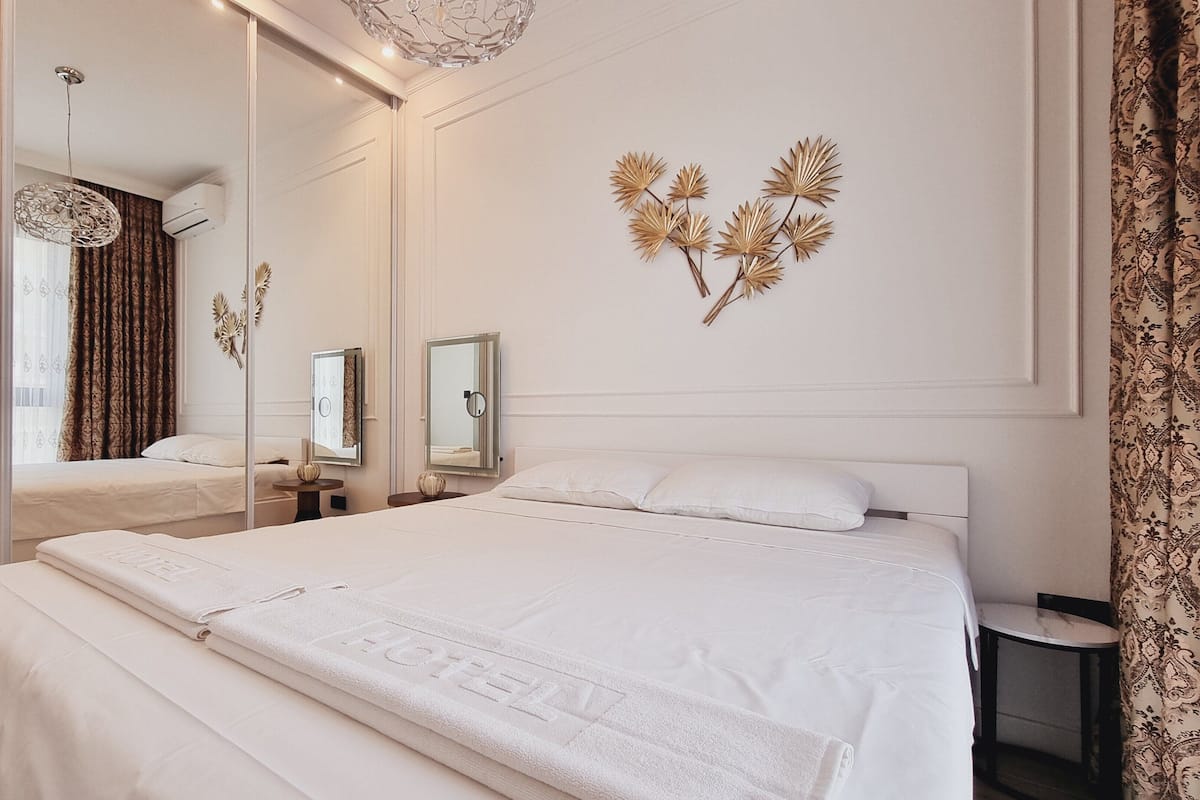 Quarto de hotel com duas camas, um espelho grande, um objeto decorativo na parede e um lustre.