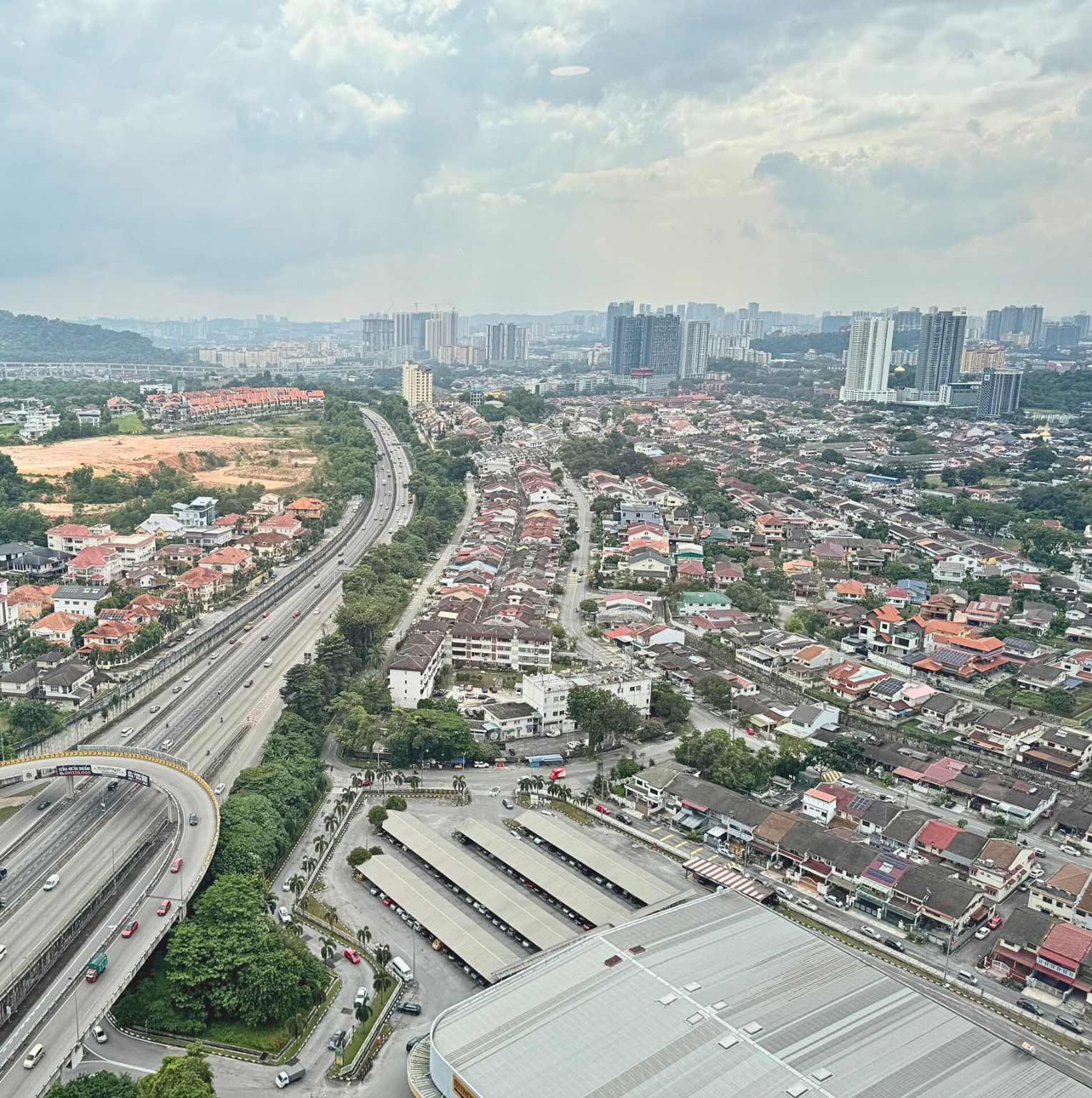Vista aérea de um horizonte urbano com edifícios residenciais e comerciais, uma autoestrada e uma grande área industrial.