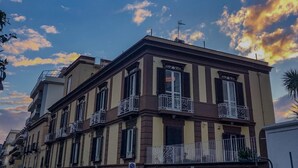 Um edifício com vários andares e varandas, uma rua em frente e um céu claro com nuvens.