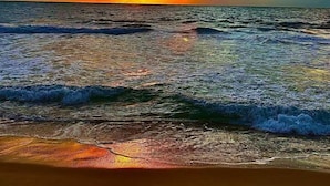 Uma praia com ondas, um pôr do sol e nuvens.