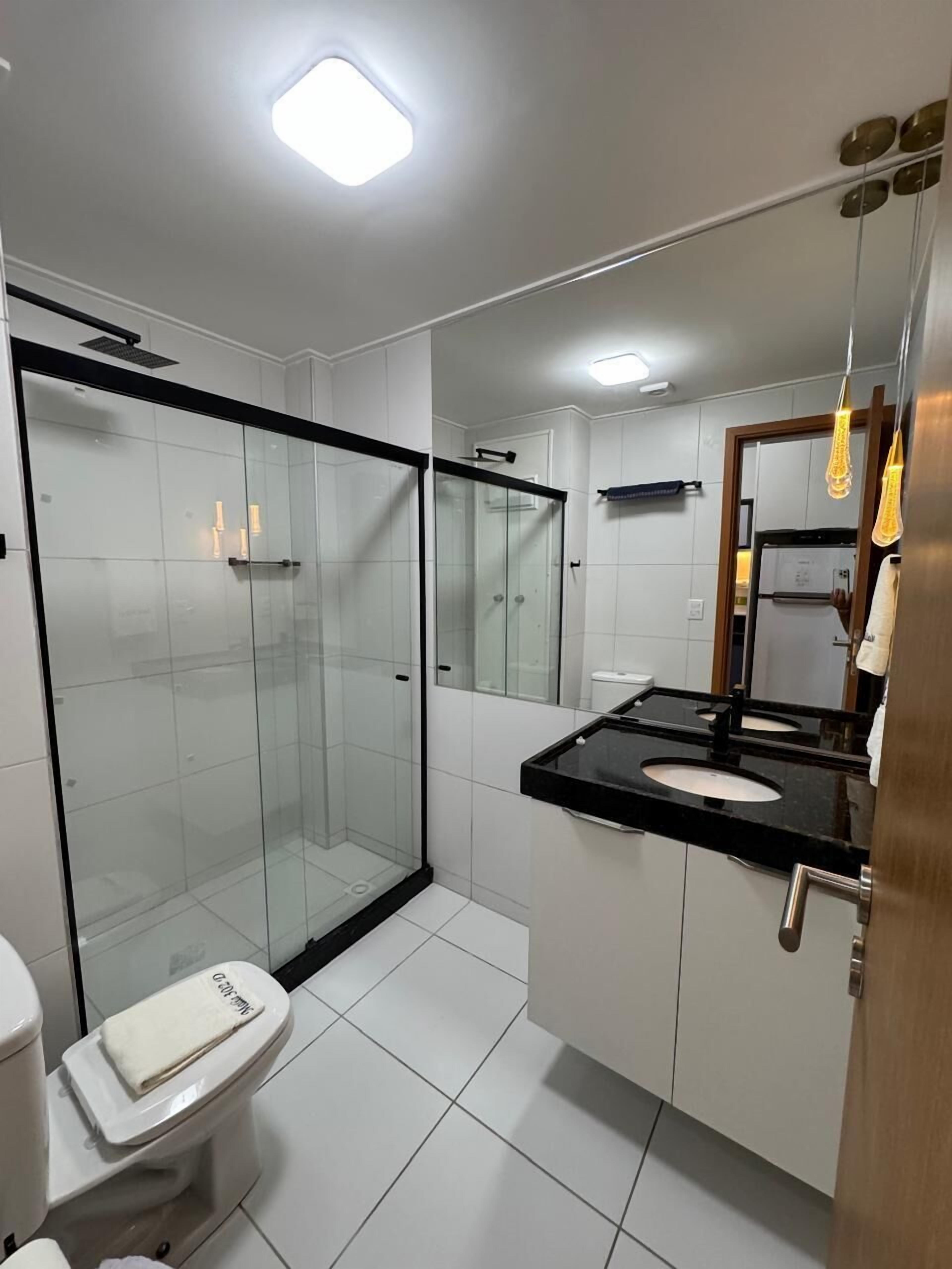 Uma casa de banho moderna com chuveiro em cabine de vidro, sanita branca e lavatório com bancada preta.