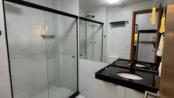 Uma casa de banho moderna com chuveiro em cabine de vidro, sanita branca e lavatório com bancada preta.