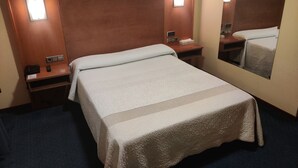 Quarto de hotel com cama, mesa de cabeceira, espelho e luminária na parede.