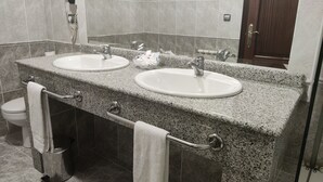 Casa de banho com duas pias, um secador de mãos, um porta-toalhas e uma sanita.