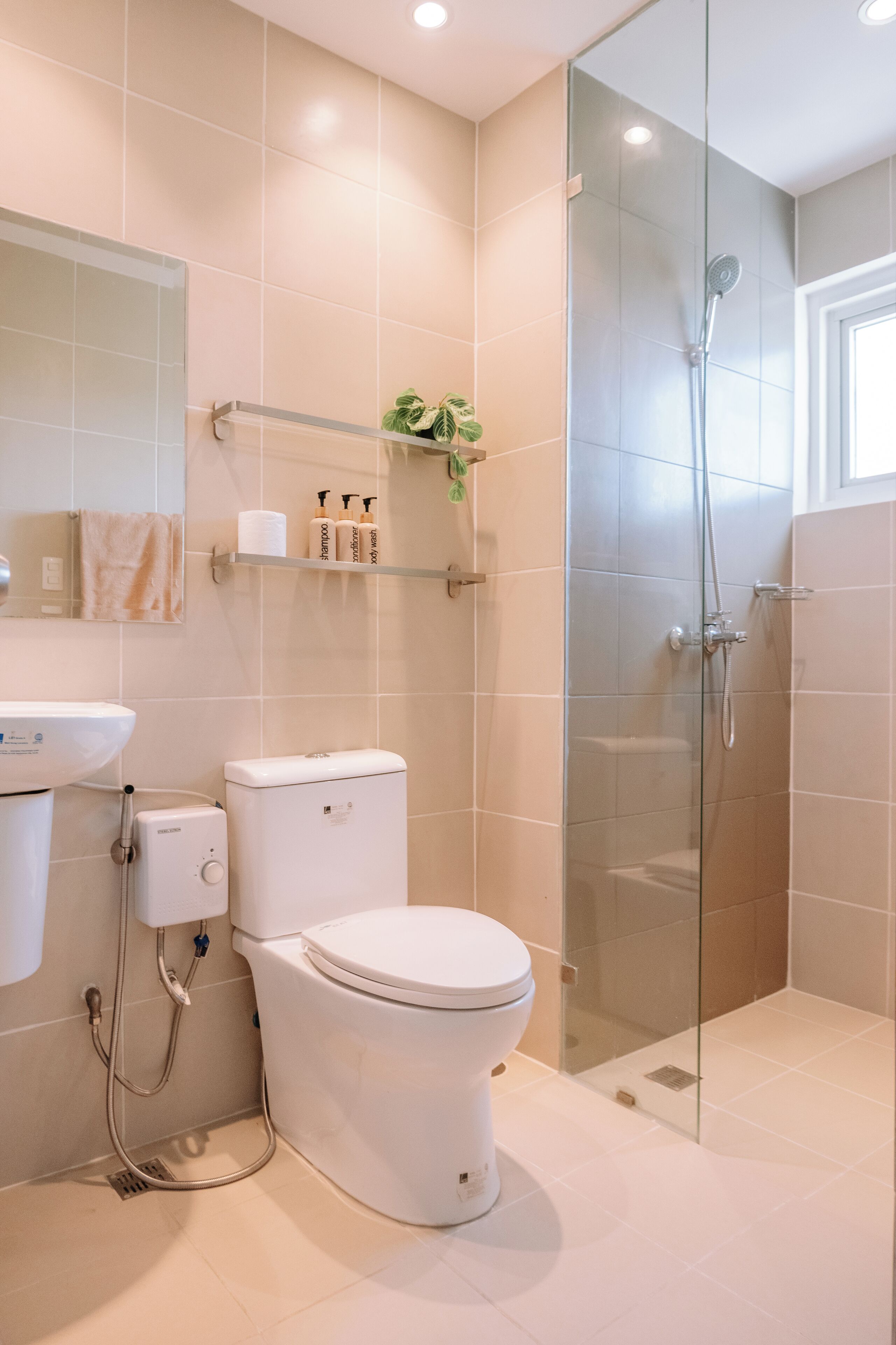 Uma casa de banho moderna com sanita, cabine de duche em vidro e prateleira com artigos de higiene pessoal.