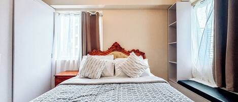 Quarto bem arrumado com uma cama grande, cabeceira de madeira e uma janela com cortinas.