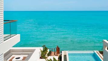 Uma área de piscina moderna com vista clara para o oceano, cadeiras de descanso e uma pessoa nadando.