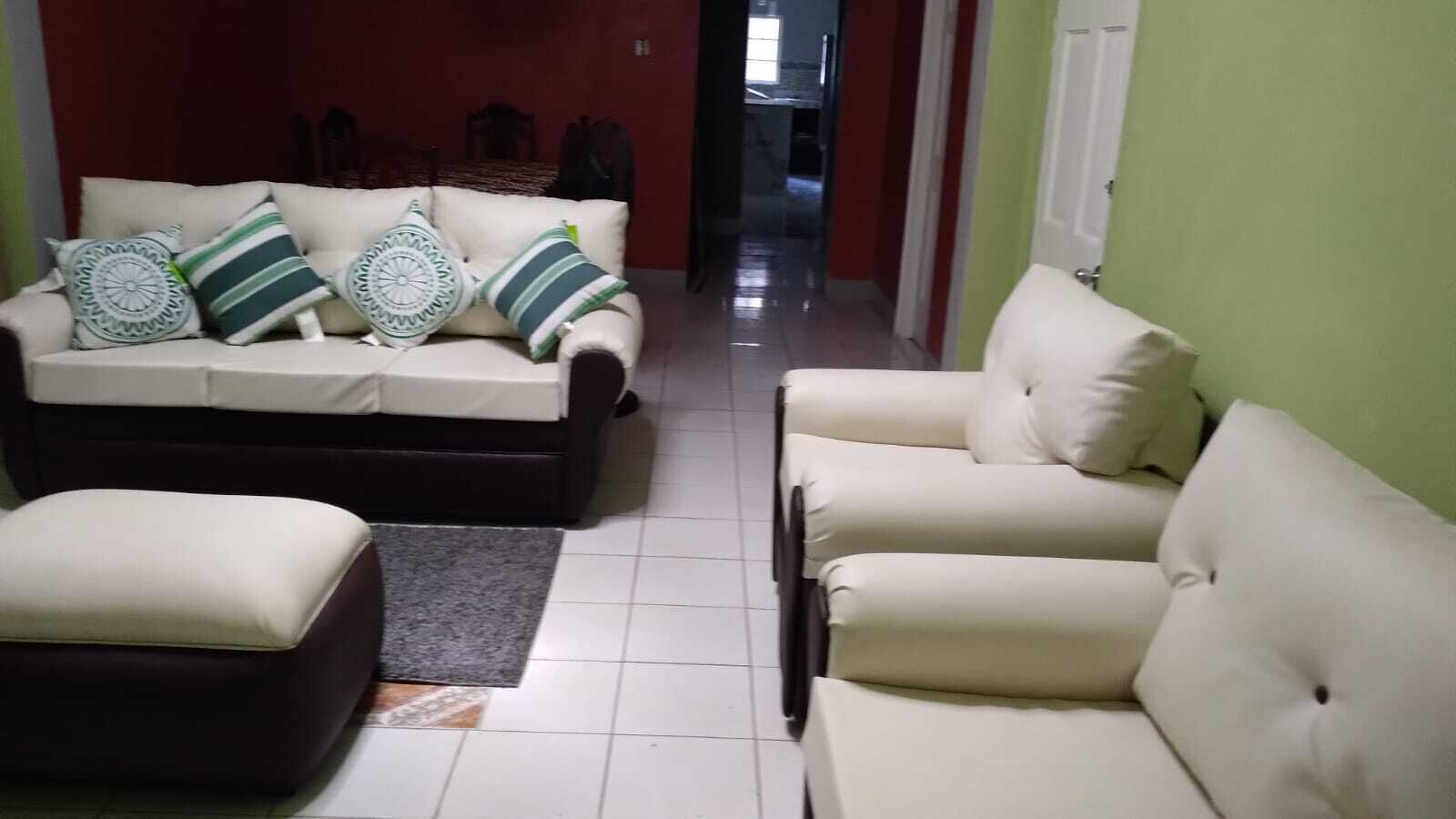 Uma sala de estar com sofá, poltrona e banqueta combinando.