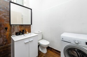 Casa de banho pequena com lavatório branco, sanita e máquina de lavar roupa com abertura frontal.