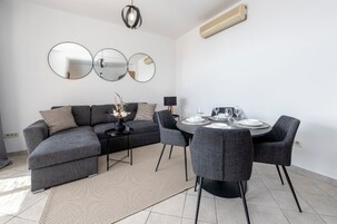Uma sala de estar moderna com um sofá seccional cinza, uma mesa de jantar redonda com quatro cadeiras e três espelhos fixados na parede.