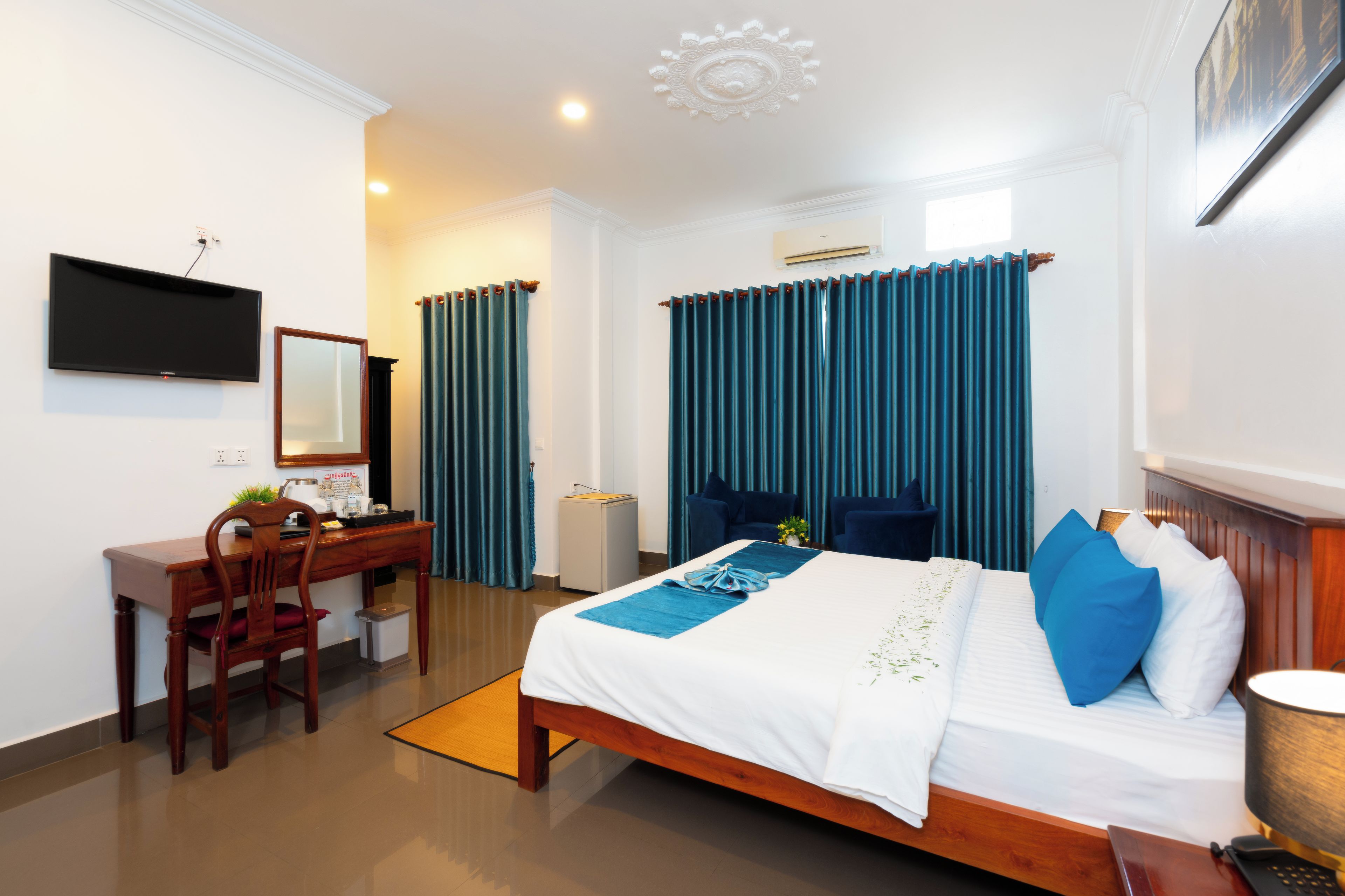 Quarto de hotel com cama, escrivaninha, cadeira, televisão e janela com cortinas.