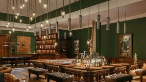 Uma área de bar com balcão de madeira, diversas luminárias pendentes e assentos de couro.