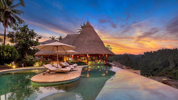 Resort com piscina, espreguiçadeiras e um edifício com telhado de palha.